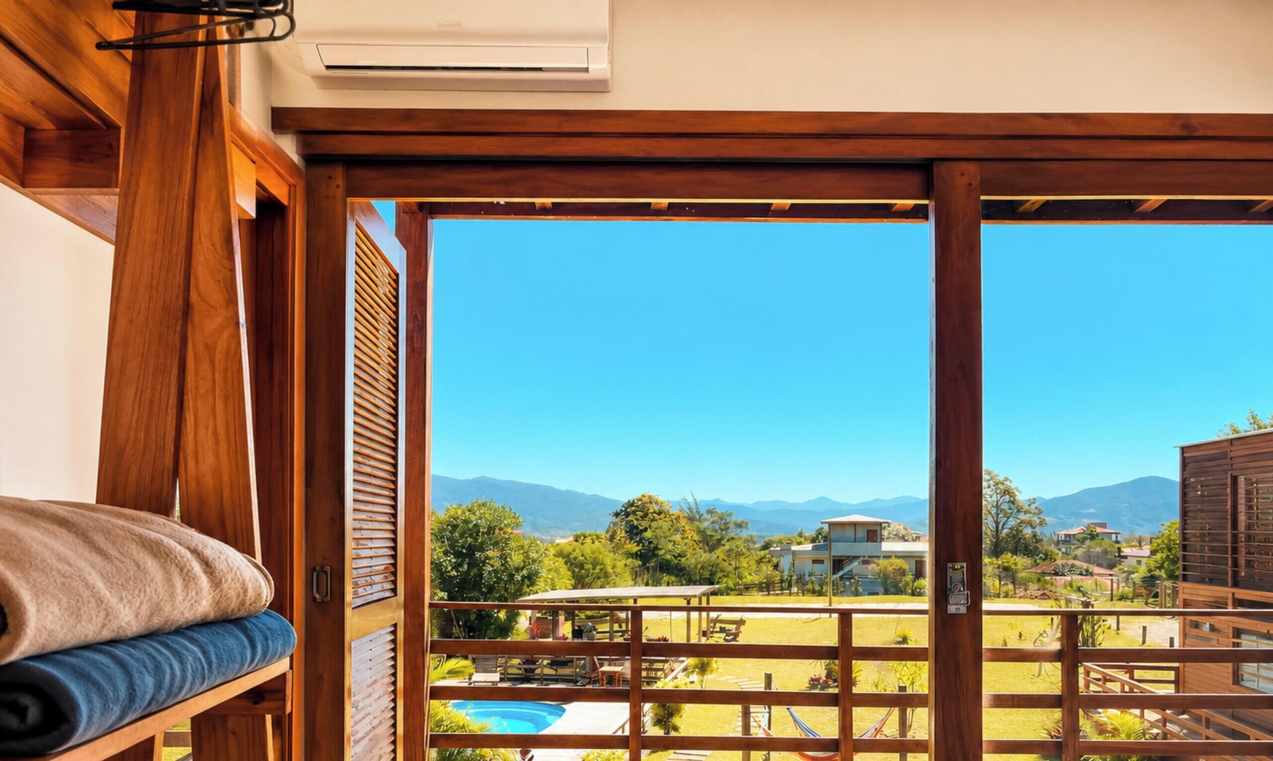 Quarto com teto de madeira, cama com manta enrolada e vista para uma piscina e montanhas.