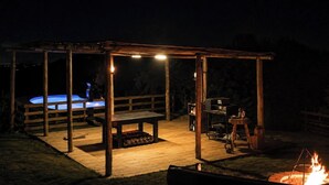 Um deck de madeira com uma banheira de hidromassagem, uma mesa e uma área de churrasco.