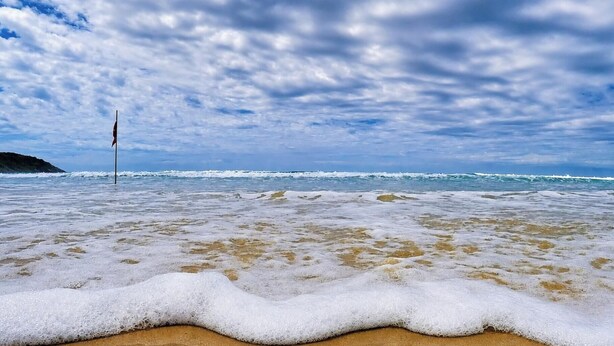 Uma praia com ondas e uma bandeira na costa.