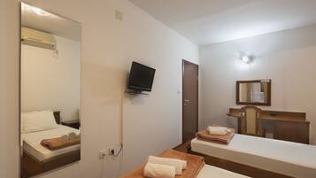 Quarto de hotel com cama, escrivaninha, televisão, espelho e porta do banheiro.