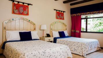 Quarto com duas camas, cada uma com colcha floral e almofadas combinando, luminária de cabeceira, telefone na mesinha de cabeceira e janela com cortinas vermelhas.