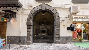 Uma entrada com arco de pedra para um edifício, com um portão de metal, uma placa com 'SD Blossom' e uma loja com roupas expostas.