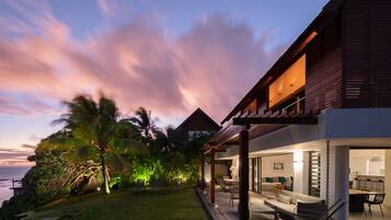 Uma casa moderna com um deck com vista para um jardim e o oceano.