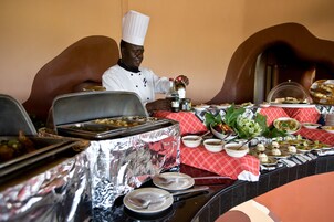 Disposição de buffet com diversos pratos e um chef preparando alimentos.