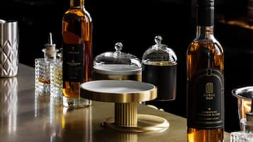 Uma área de bar com garrafas de bebidas, um copo e um recipiente de metal sobre uma superfície refletora.