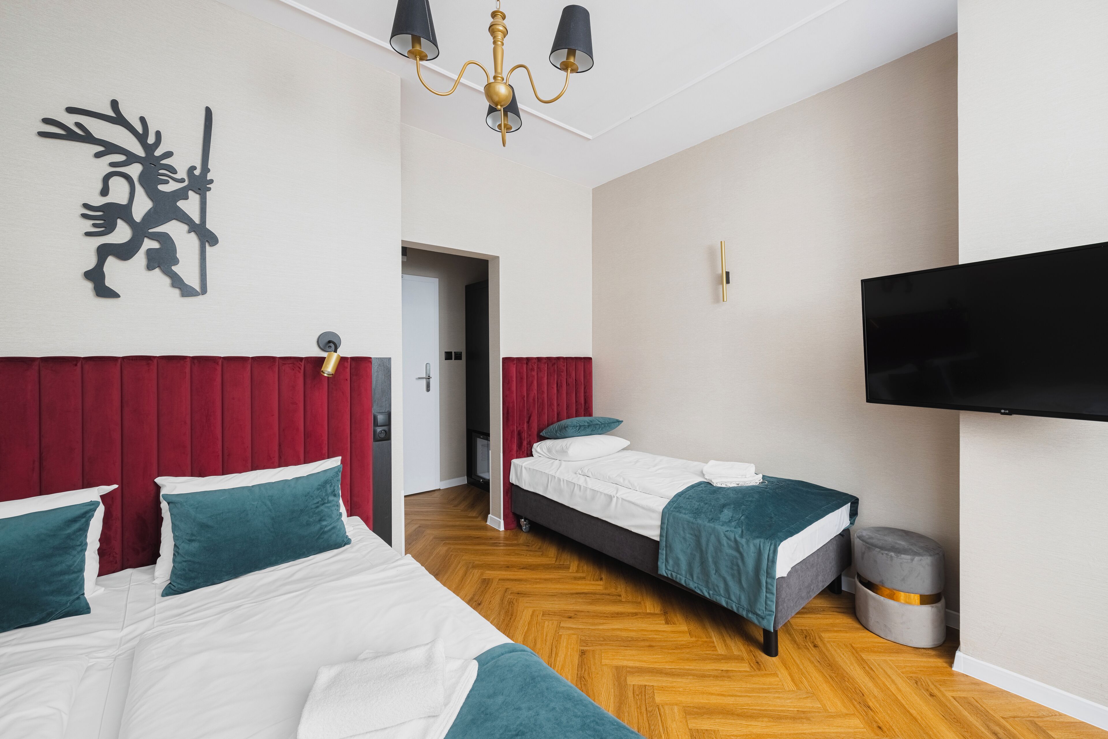 Quarto de hotel com duas camas, televisão, lustre e cortina vermelha.