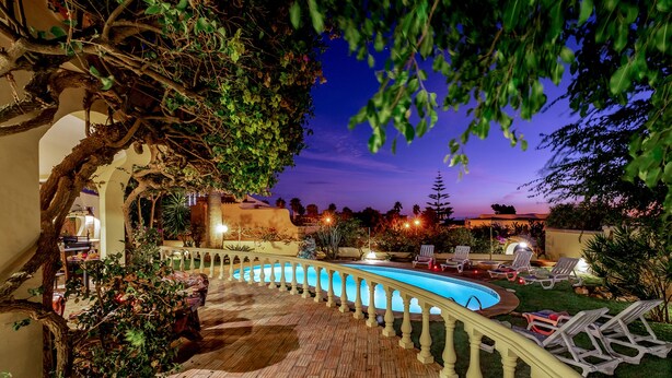 Piscina com design curvo, rodeada por um deck de madeira e um guarda-corpo branco.