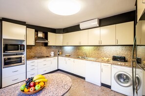 Cozinha moderna com armários brancos, bancada de granito, forno embutido, micro-ondas, torradeira e máquina de lavar roupa.