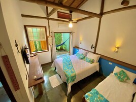 Quarto com duas camas, uma escrivaninha de madeira, rede externa e ventilador de teto.