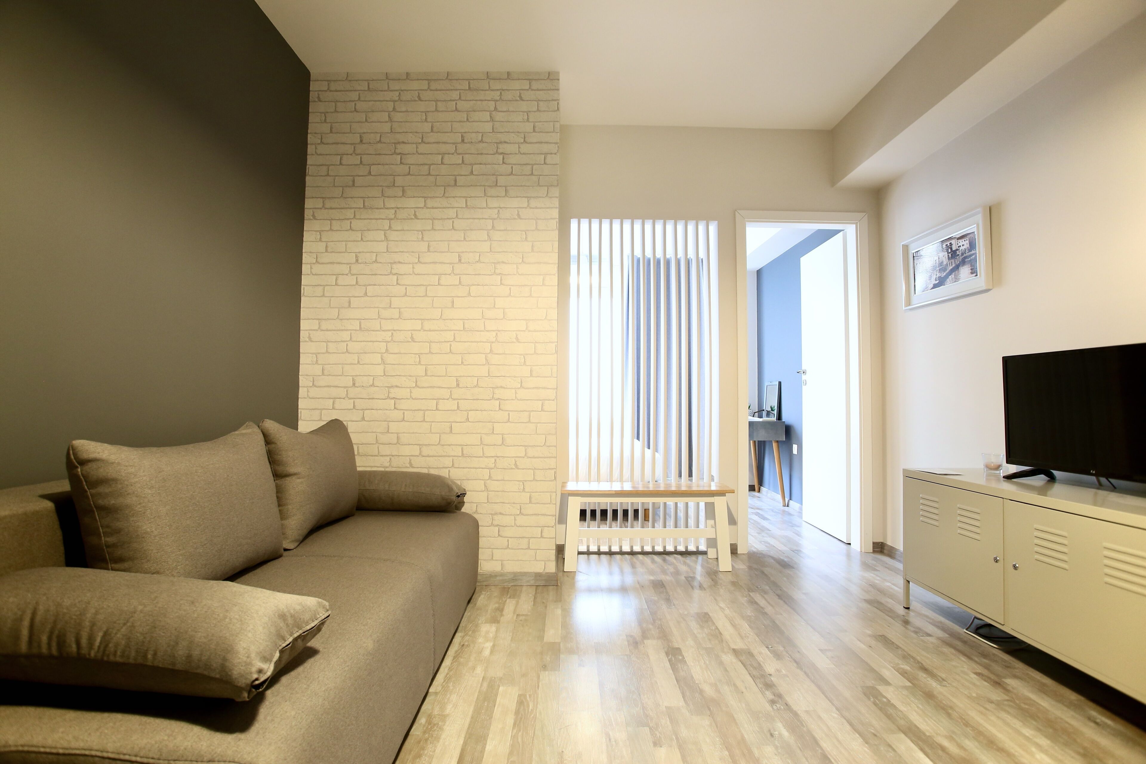 Uma sala de estar moderna com um sofá, um banquinho, uma TV e um armário.
