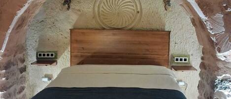 Uma cama com cabeceira de madeira, parede de pedra e um desenho circular acima.