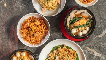 Diversos pratos asiáticos, incluindo macarrão, frutos do mar e sopa, dispostos sobre uma mesa de mármore.