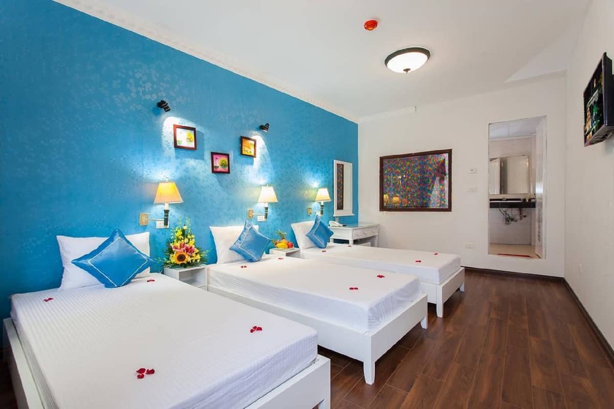 Quarto de hotel com duas camas, uma parede azul de destaque e um quadro.