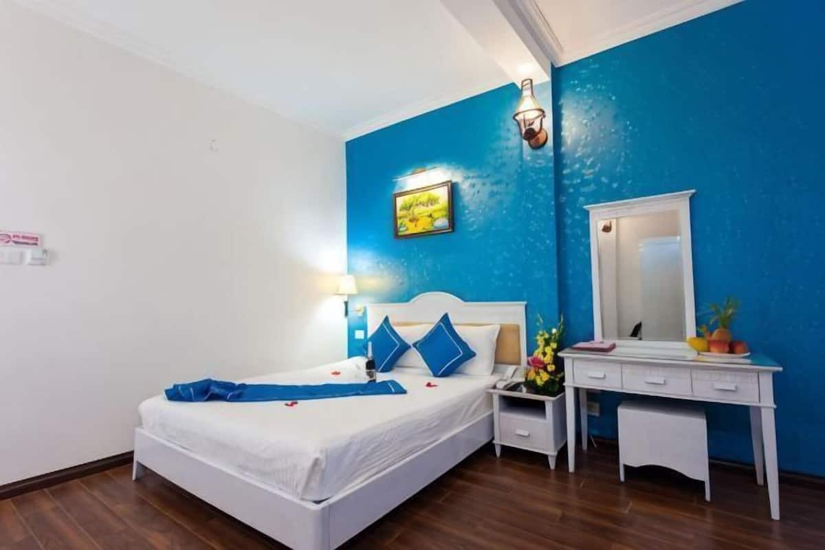 Quarto de hotel com cama, mesa de cabeceira, penteadeira e espelho.