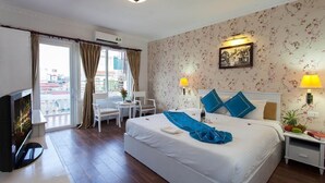 Quarto de hotel com cama, abajures, televisão, mesinha e uma cadeira.