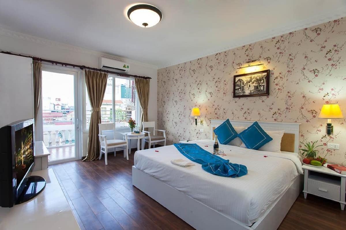 Quarto de hotel com cama, abajures, televisão, mesinha e uma cadeira.
