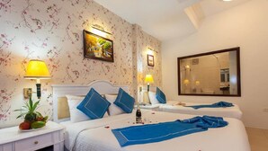 Quarto de hotel com duas camas, papel de parede floral, abajures, um espelho grande e uma pequena planta no criado-mudo.