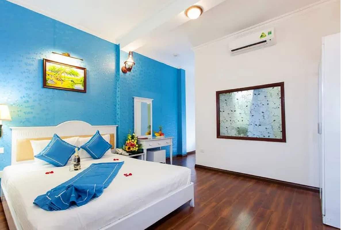 Quarto de hotel com uma cama grande, uma escrivaninha, uma cadeira, um espelho e uma janela com vista para o exterior.