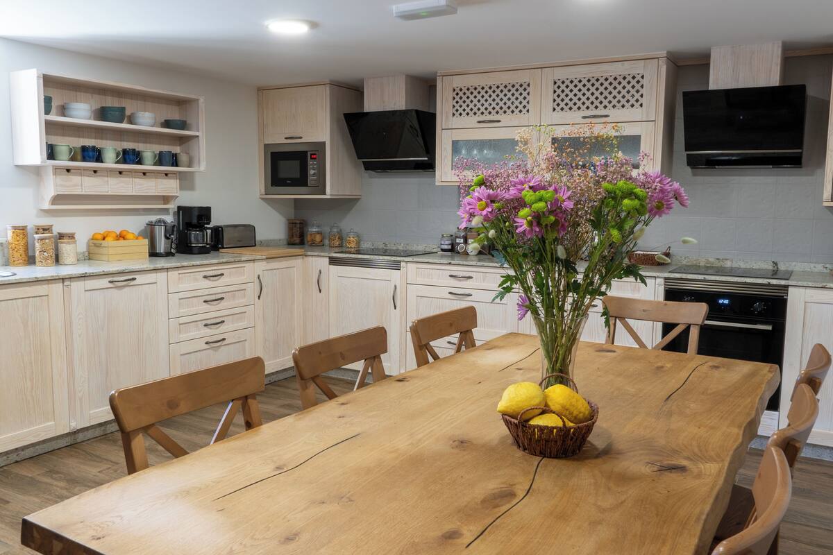 Uma cozinha moderna com armários de madeira, uma mesa de jantar com cadeiras, uma televisão e um vaso com flores e limões.