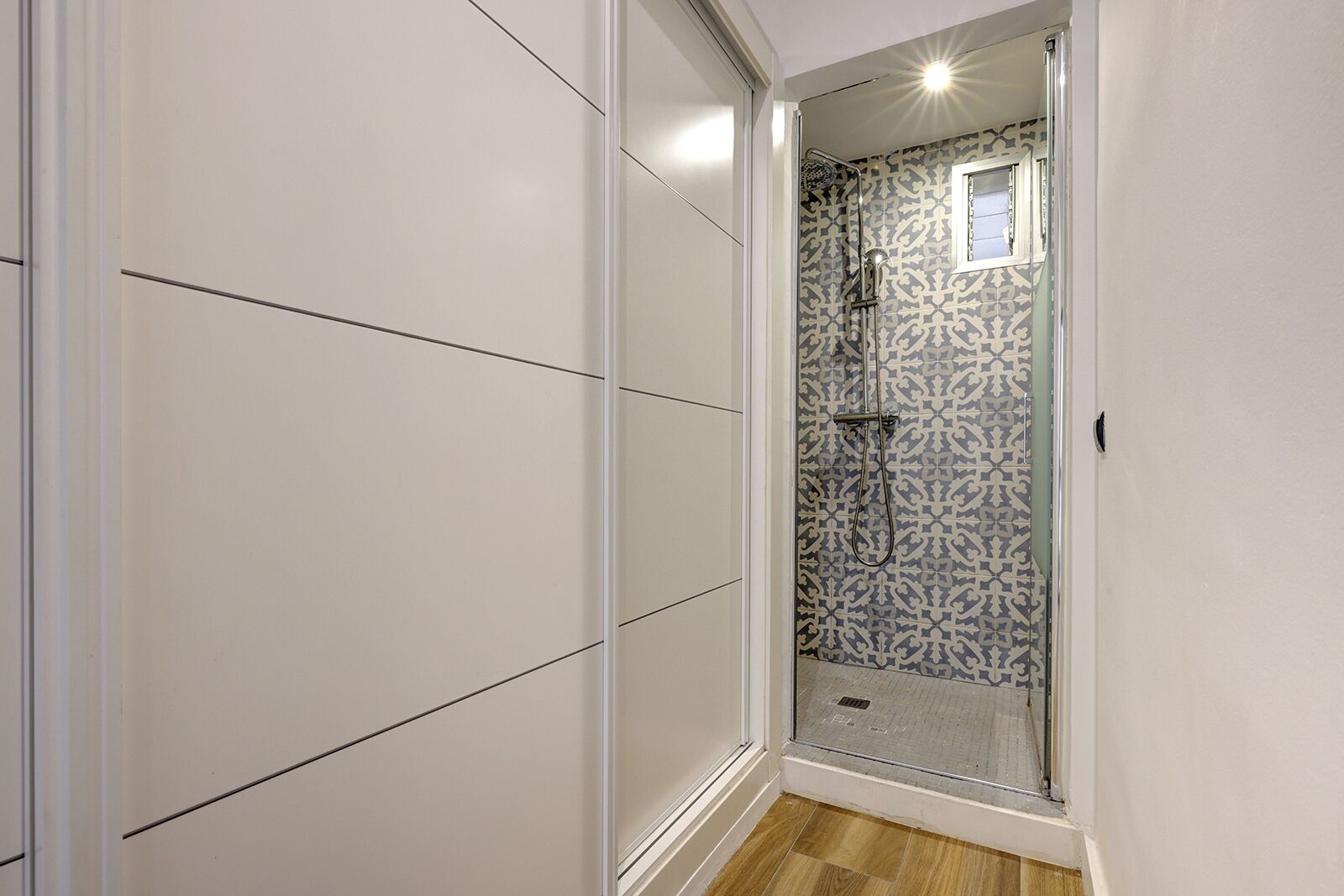 Um corredor estreito com área de chuveiro, azulejos estampados e porta de vidro.