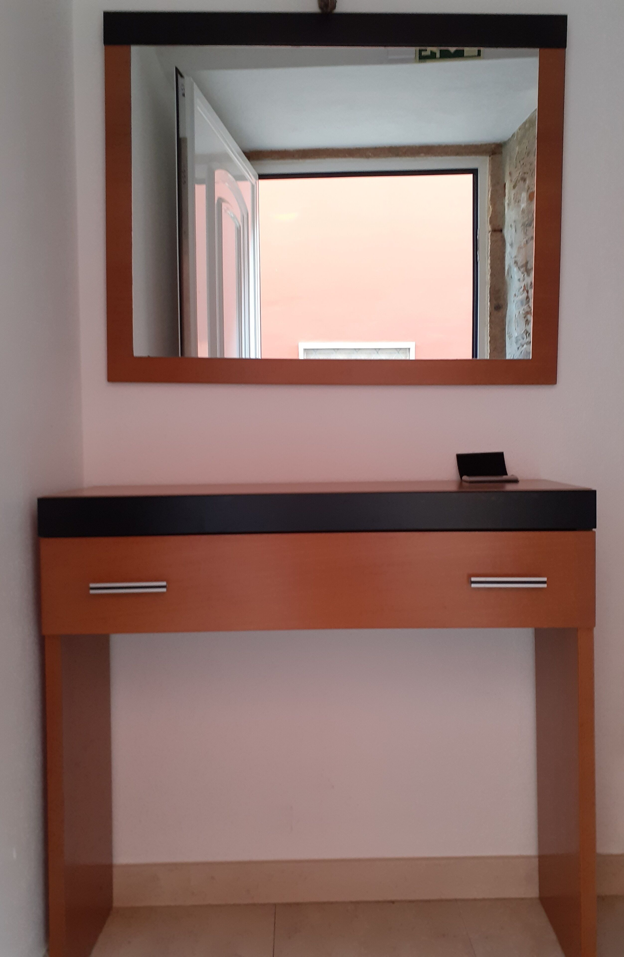 Uma toucador de banheiro com espelho, duas gavetas e uma pequena prateleira.