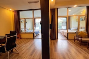 Quarto de hotel com piso de madeira, uma escrivaninha com cadeira, duas camas e janelas amplas com cortinas.