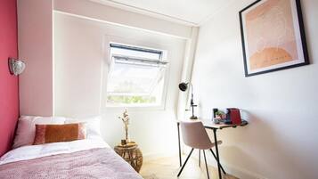 Quarto com cama, escrivaninha, cadeira, janela e luminária fixa na parede.