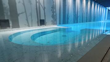 Piscina interior moderna com piso e paredes de mármore, destacando silhuetas de árvores.