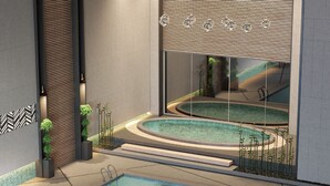 Um edifício moderno com área de piscina, incluindo uma piscina circular e uma piscina retangular, cercado por plantas e um muro de ripas de madeira.