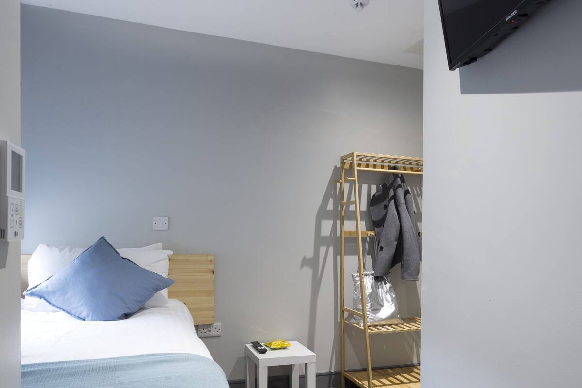 Quarto de hotel com uma cama, uma mesinha, uma televisão e uma cama beliche com uma jaqueta pendurada.