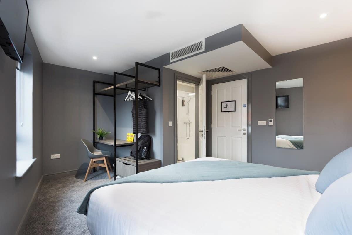 Quarto moderno com cama, escrivaninha e área de chuveiro.