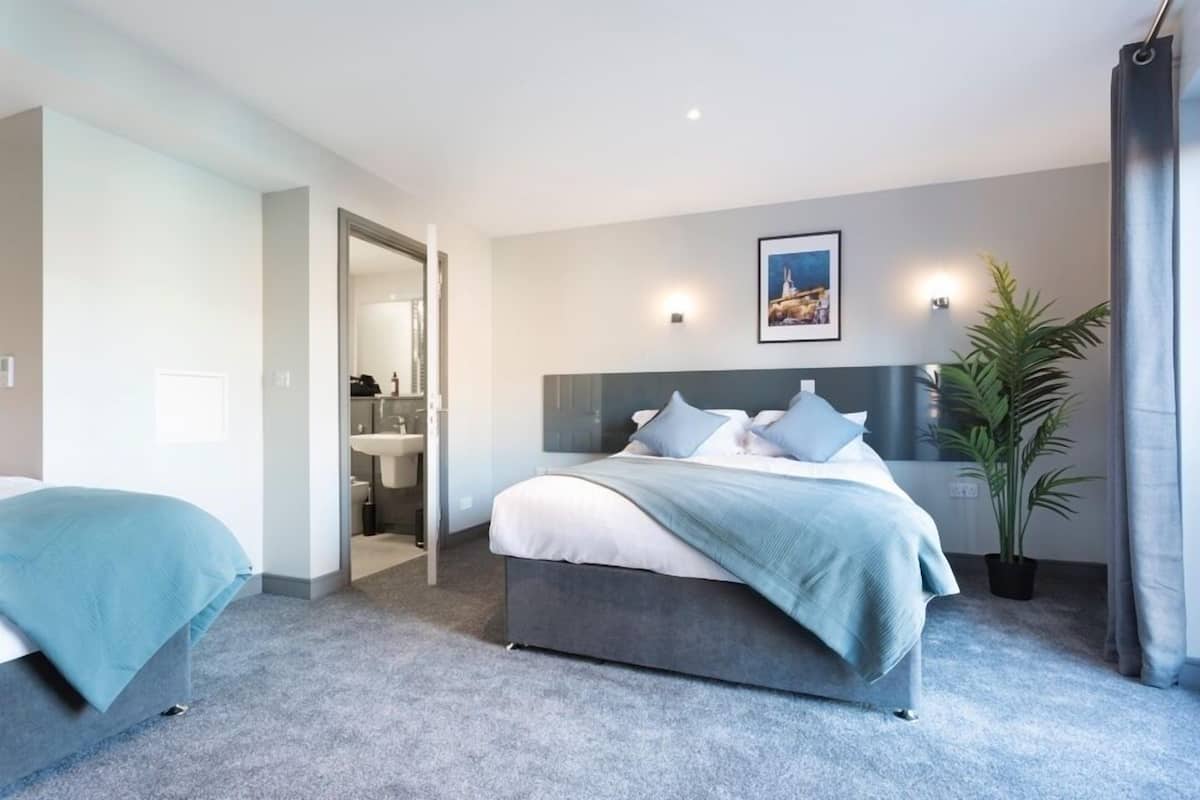 Quarto de hotel moderno com uma cama grande, mesa de cabeceira, espelho e planta em vaso.
