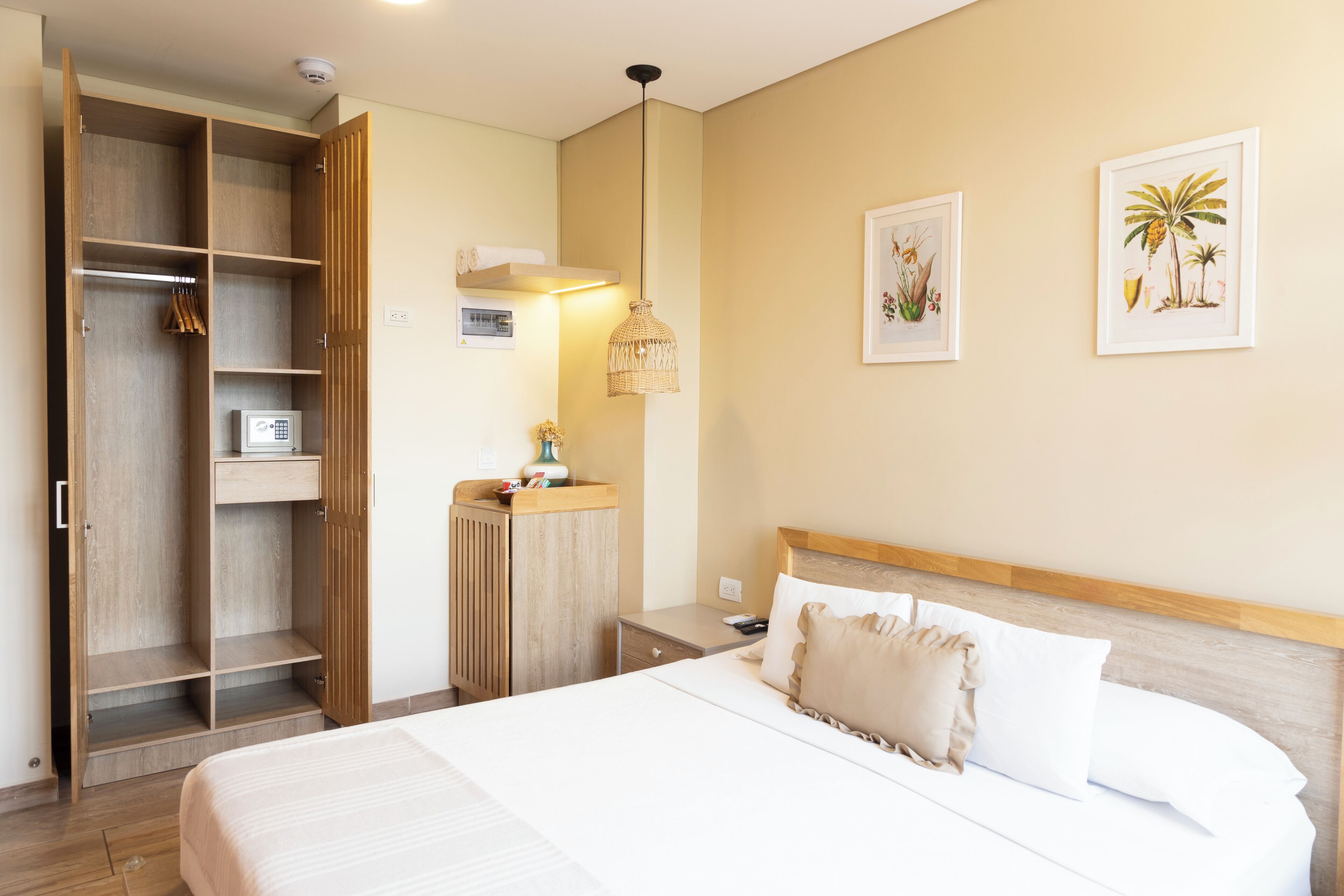Quarto de hotel com cama, guarda-roupa, mesa de cabeceira e prateleira na parede.