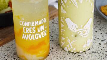 Dois cocktails sobre um balcão salpicado, com um prato de comida ao fundo.