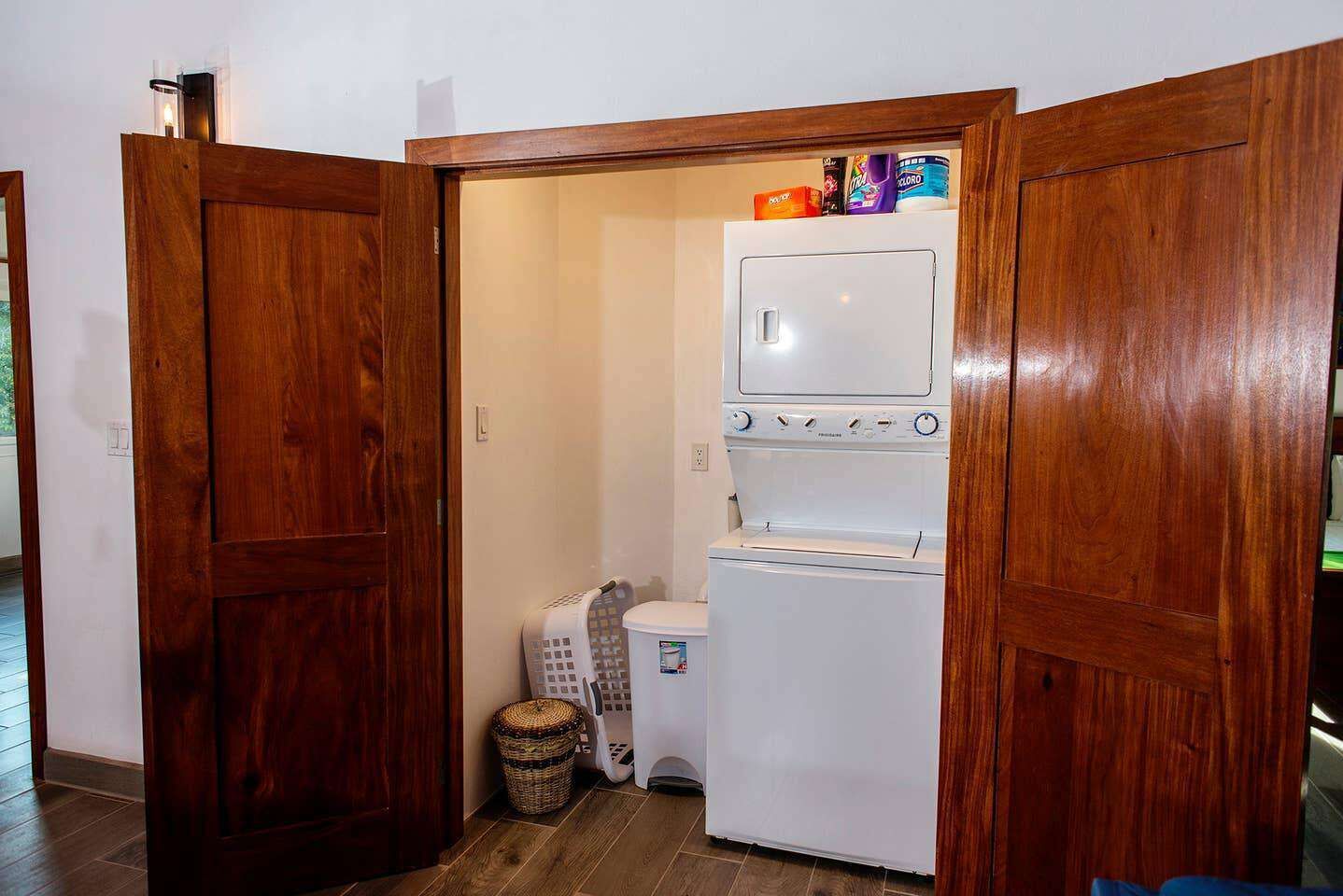 Uma lavanderia compacta com máquina de lavar e secadora embutidas, portas de madeira e uma pequena cesta.