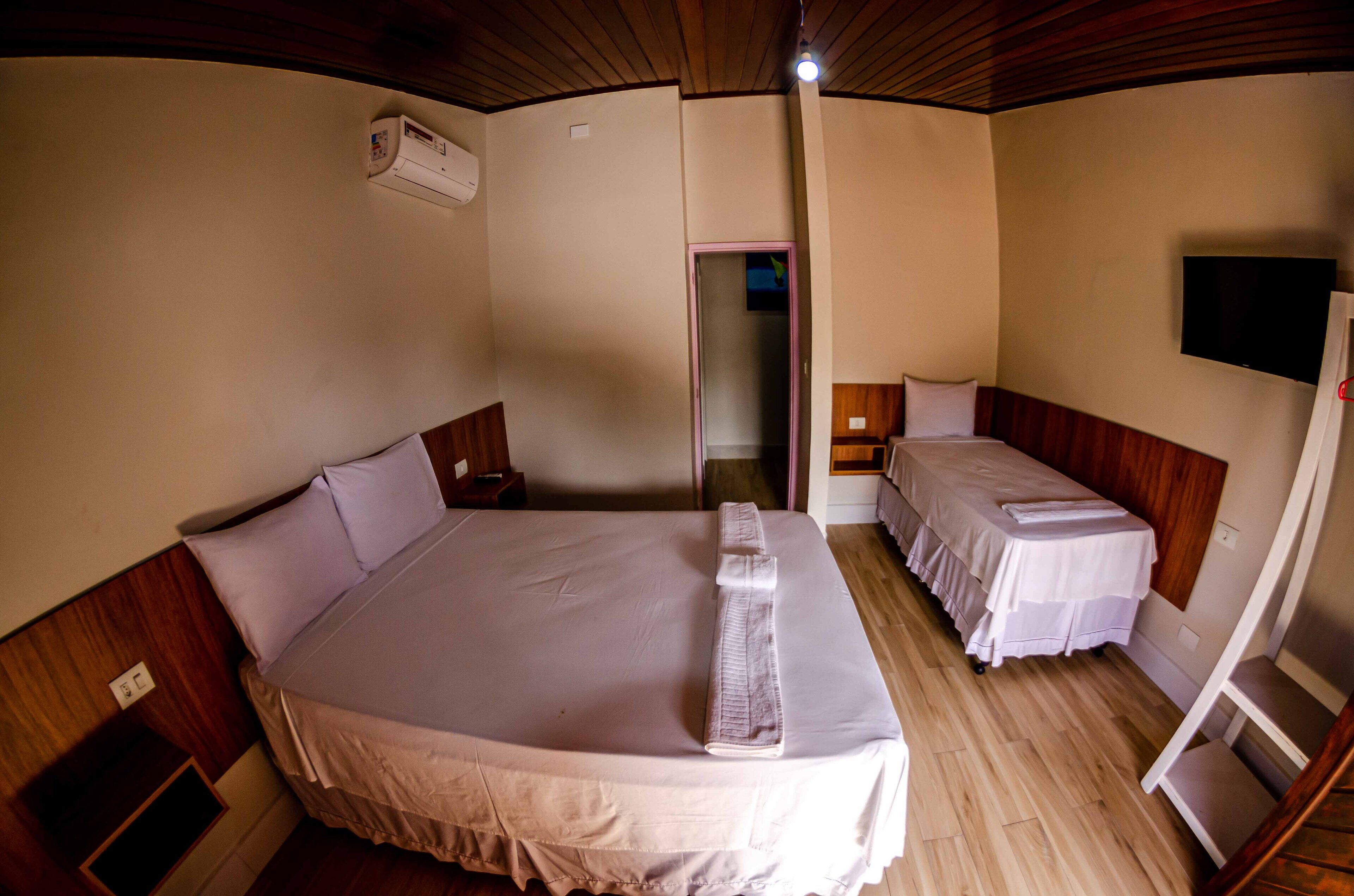 Quarto de hotel com uma cama grande, duas camas menores, uma televisão e um ar condicionado.