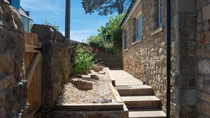 Pátio com paredes de pedra e escadaria de madeira que leva a uma porta.