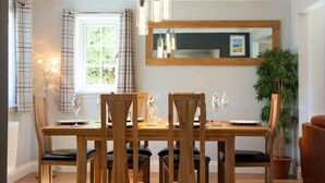 Uma sala de jantar com mesa e cadeiras de madeira, um espelho grande acima da mesa e um vaso com planta ao lado.