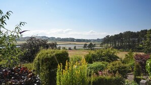 Um jardim com diversas plantas e vista para uma paisagem distante, incluindo campos e árvores.