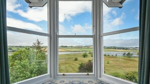 Quarto com uma janela ampla que oferece vista para uma paisagem rural, incluindo campos e um corpo d'água.