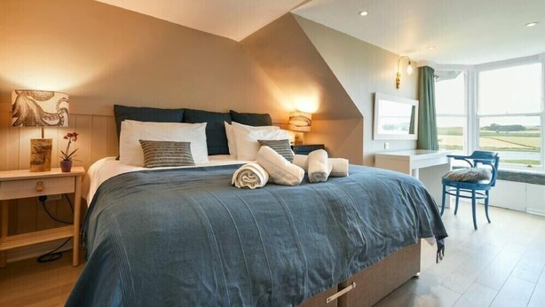 Quarto com cama grande, mesas de cabeceira, escrivaninha e uma cadeira.