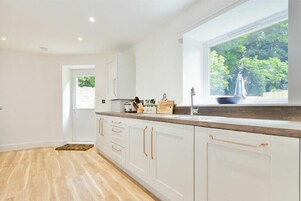 Uma cozinha moderna com armários brancos, bancada de madeira e janela com vista para o verde.