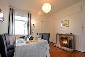 Uma sala de jantar com uma mesa posta para dois, lareira e janela com cortinas.