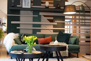 Uma sala de estar moderna com um sofá verde, uma mesa de centro redonda e um painel decorativo na parede.