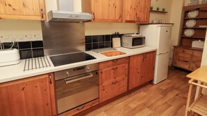 Cozinha compacta com armários de madeira, coifa de aço inoxidável, micro-ondas e geladeira.