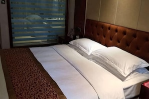 Quarto de hotel com cama, cabeceira, mesa de cabeceira e janela com persianas.