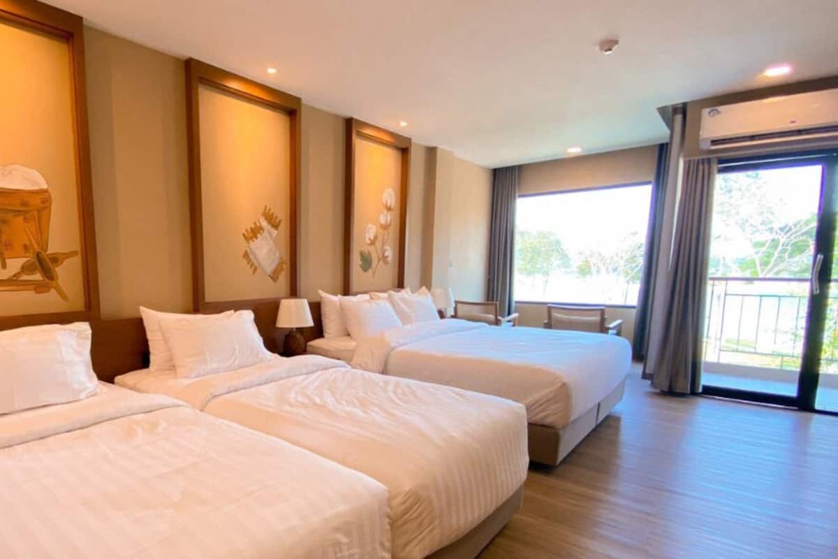 Quarto de hotel com três camas, uma janela grande com vista e obras de arte nas paredes.