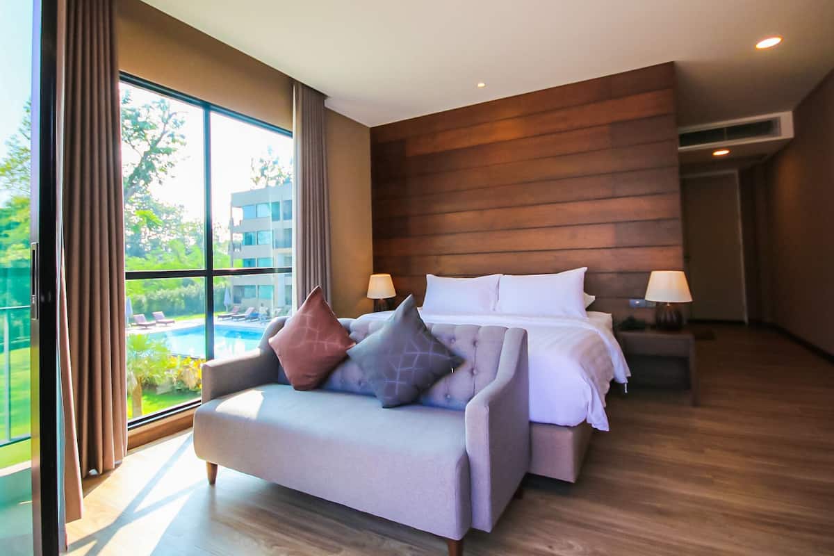 Quarto de hotel moderno com uma cama grande, um sofá e vista para uma piscina.