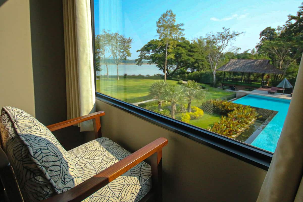 Quarto com vista para uma piscina, uma cadeira e uma janela com cortinas.