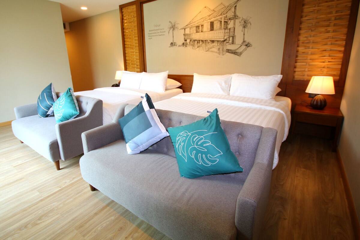 Quarto de hotel com duas camas, um sofá cinzento e uma parede de madeira com um mural.
